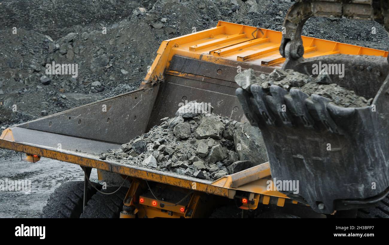 Excavator fills dump truck. Bucket excavator closeup loads stones into ...