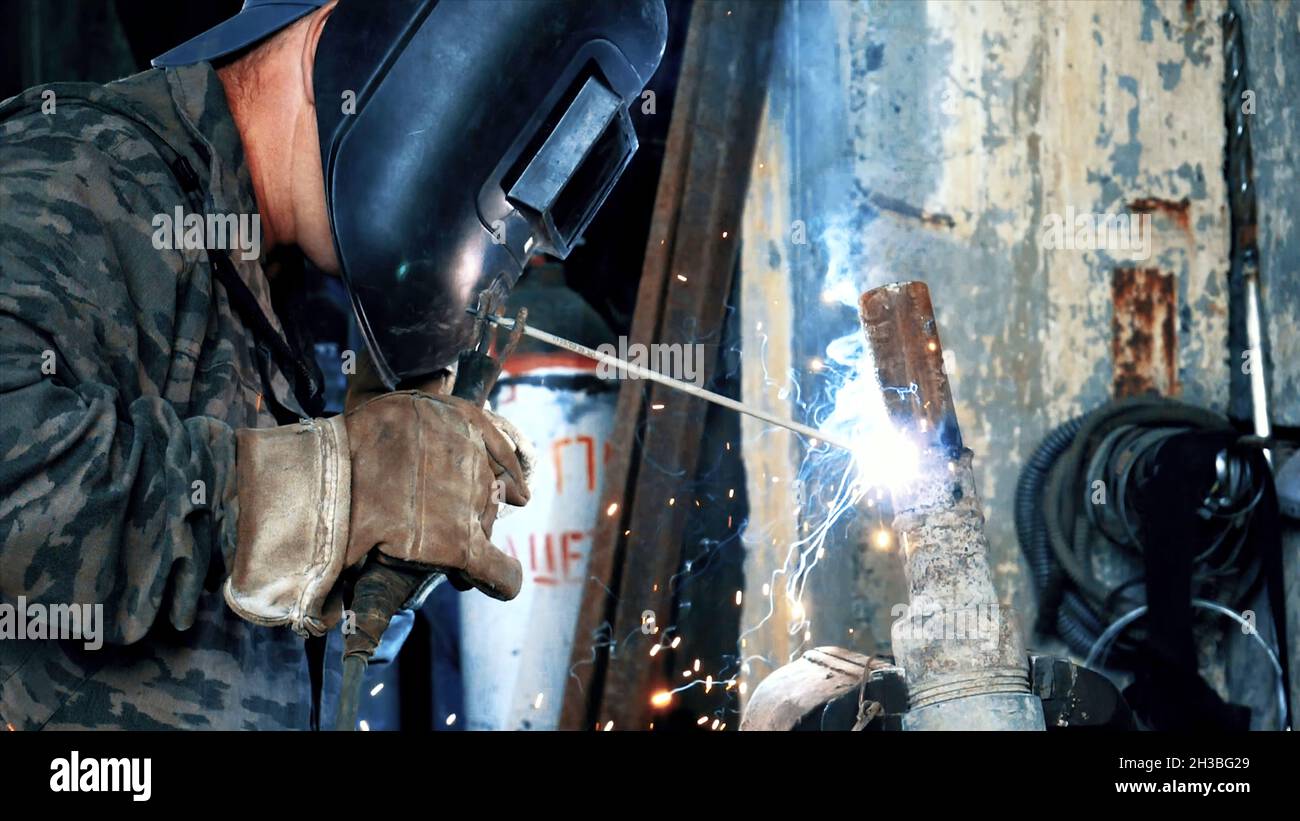 Welder at the factory in welding mask welds metal parts. Frame. Masked ...