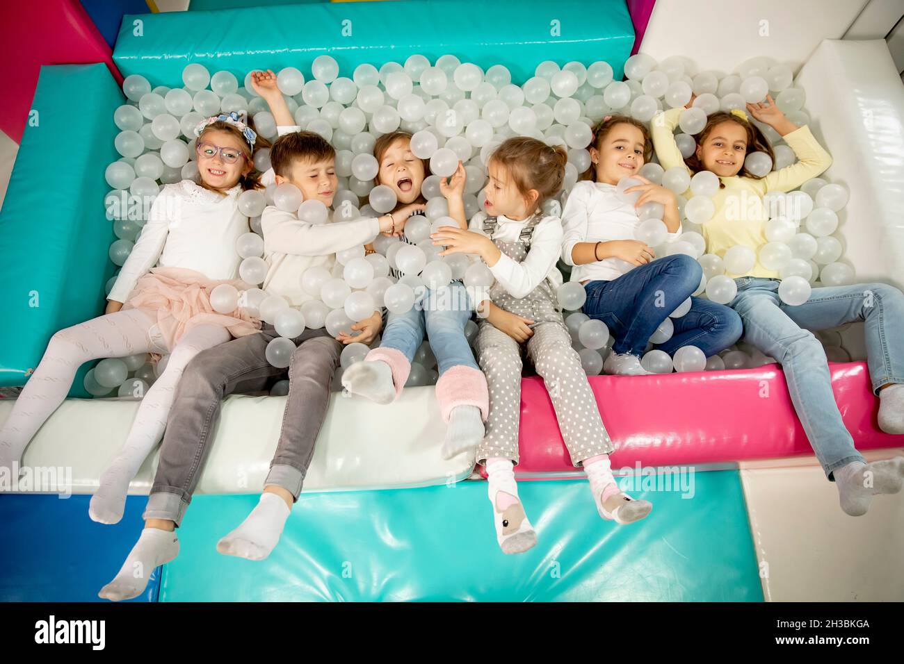 Group of happy little kids in ball pit smiling happily at camera while ...