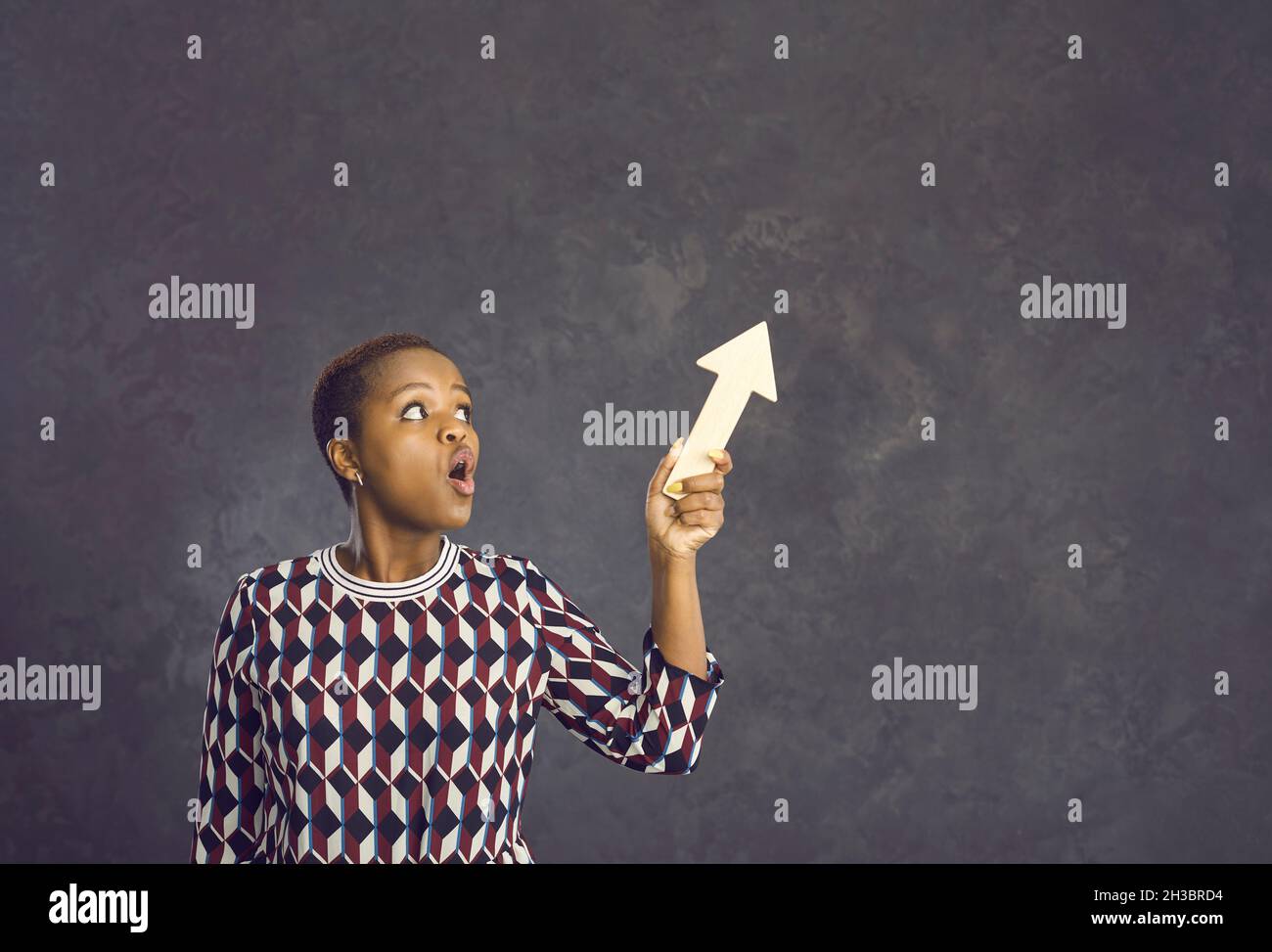 Shocked young african american woman with wooden arrow pointing up ...