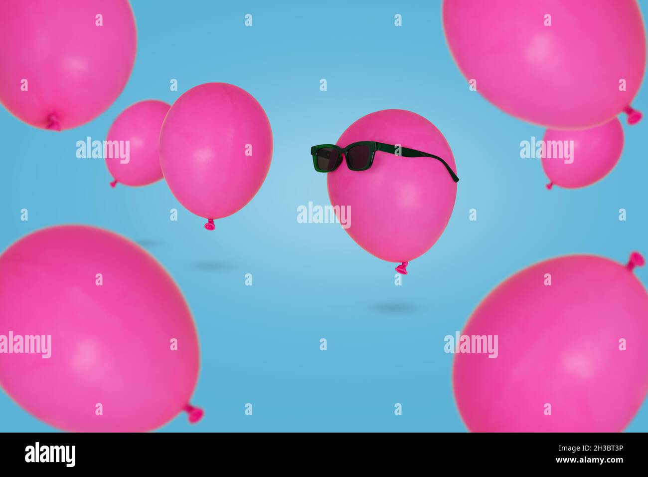 Pink balloon in sunglasses floating in the air with other balloons ...