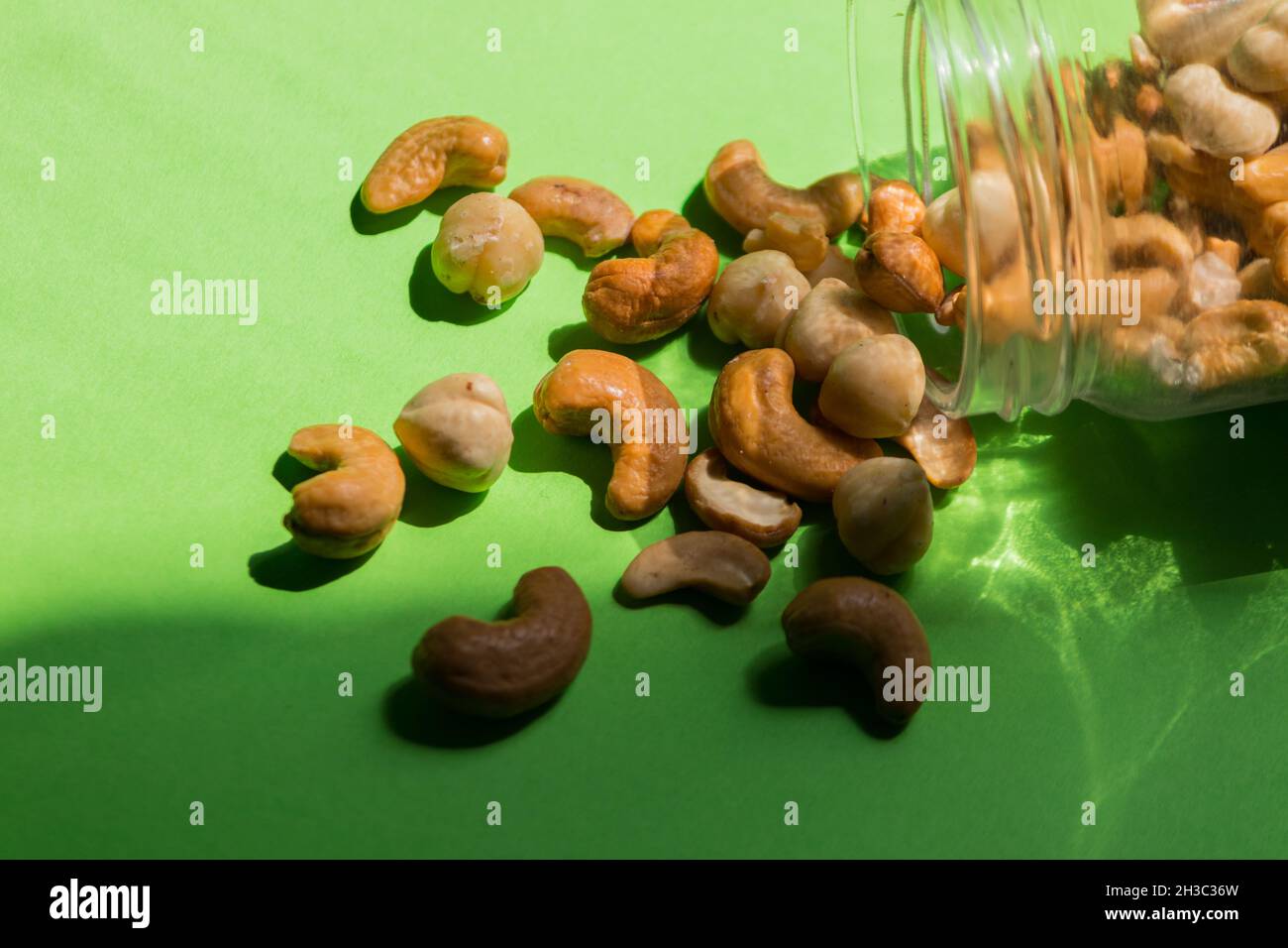 Scattered nuts from a glass jar on a green background. Hazelnuts and ...