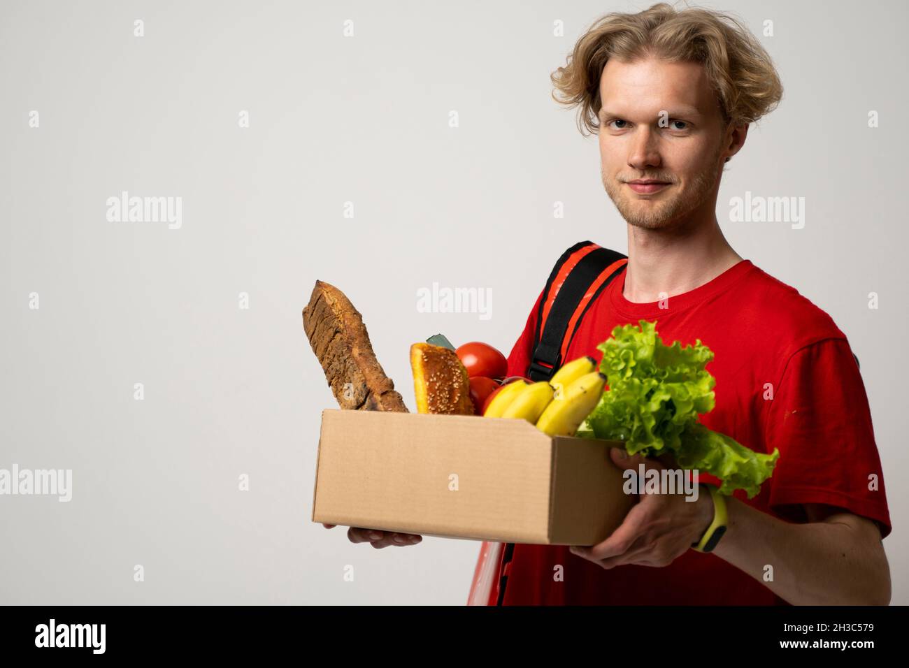 Portrait of smiling handsome delivery man holding paper grocery box ...