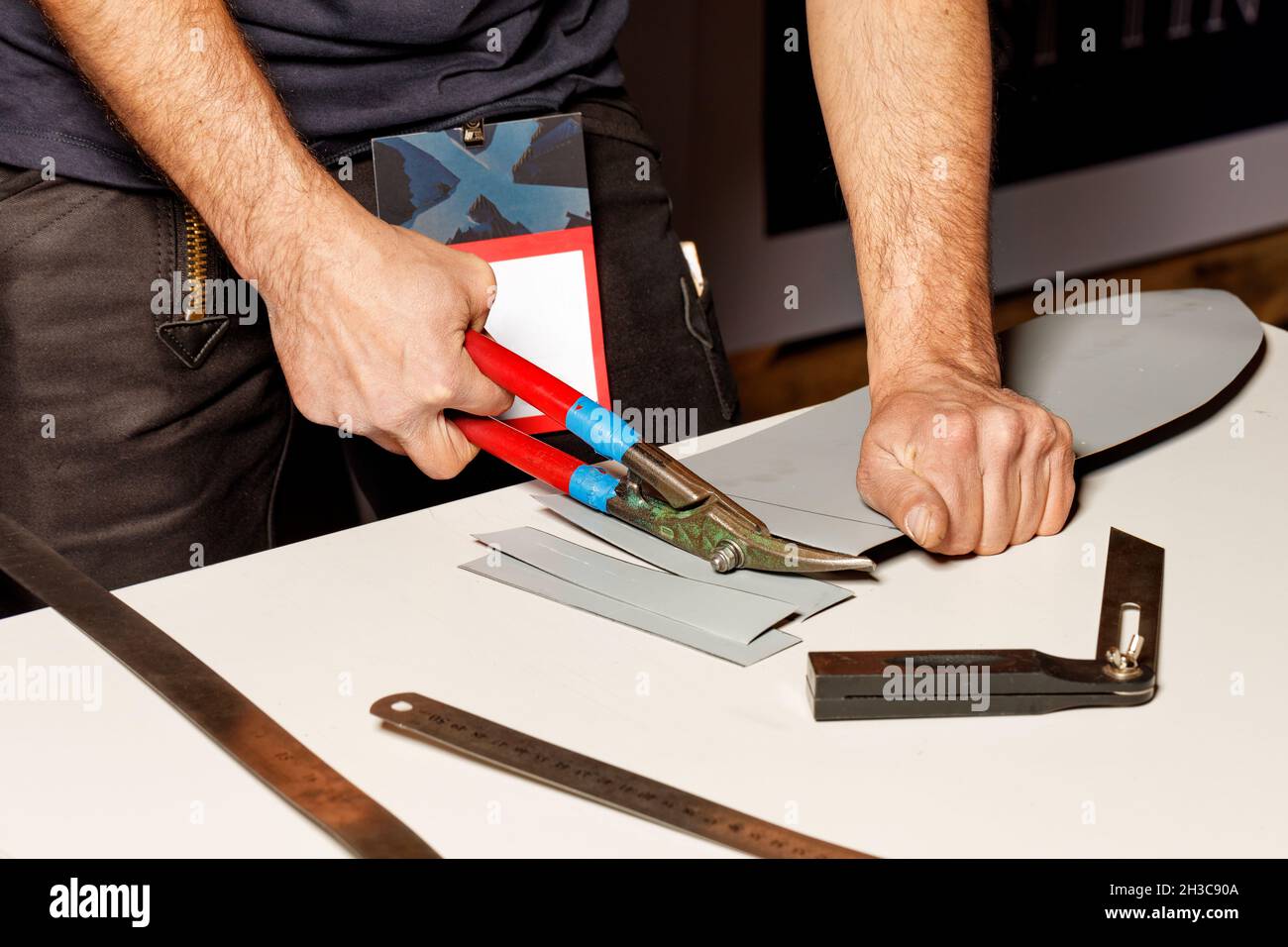 The male hands of a worker cut a sheet of roofing iron with metal ...