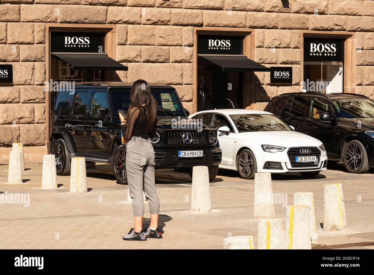 Lone young woman and expensive cars outside Hugo Boss official store in ...