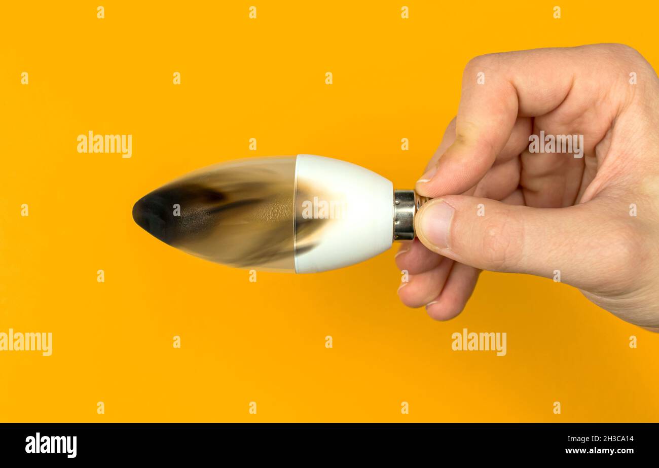 Hand with broken after fire LED light bulb. Concept of electrical short ...