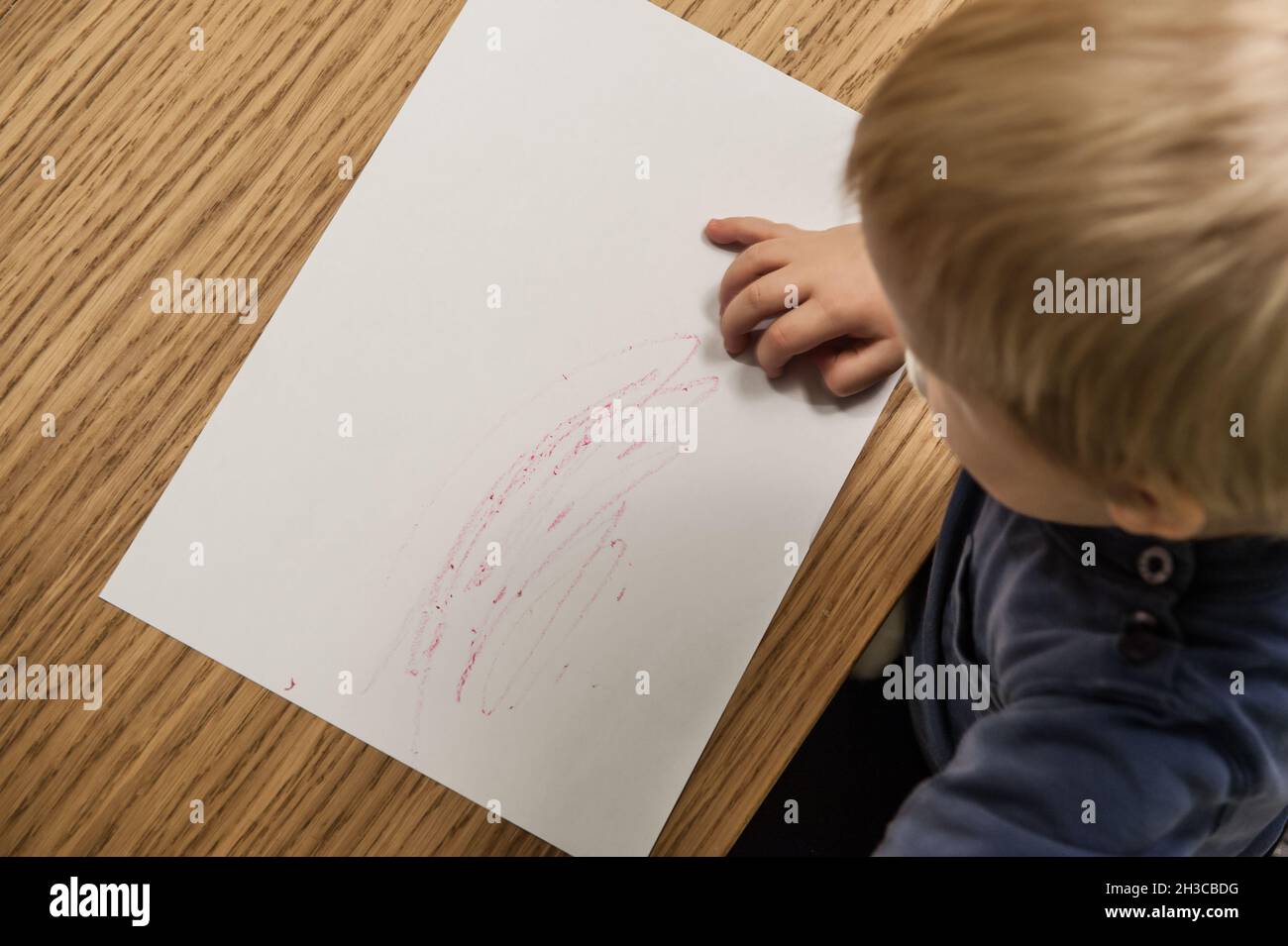 Small kid drawing with a red crayon on a white piece of paper Stock ...