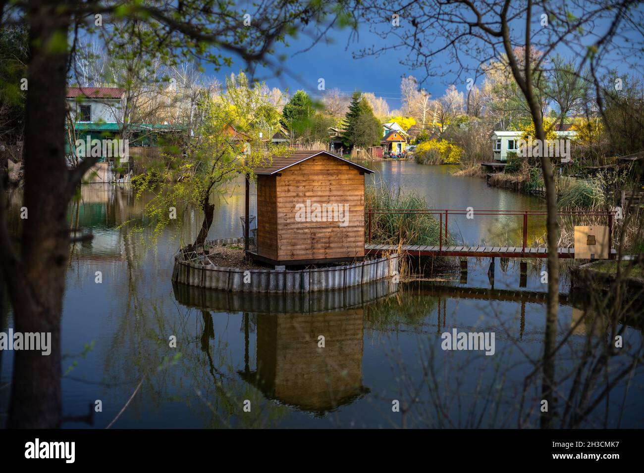 Wooden shed with a small bridge on a lake framed by tree branches ...