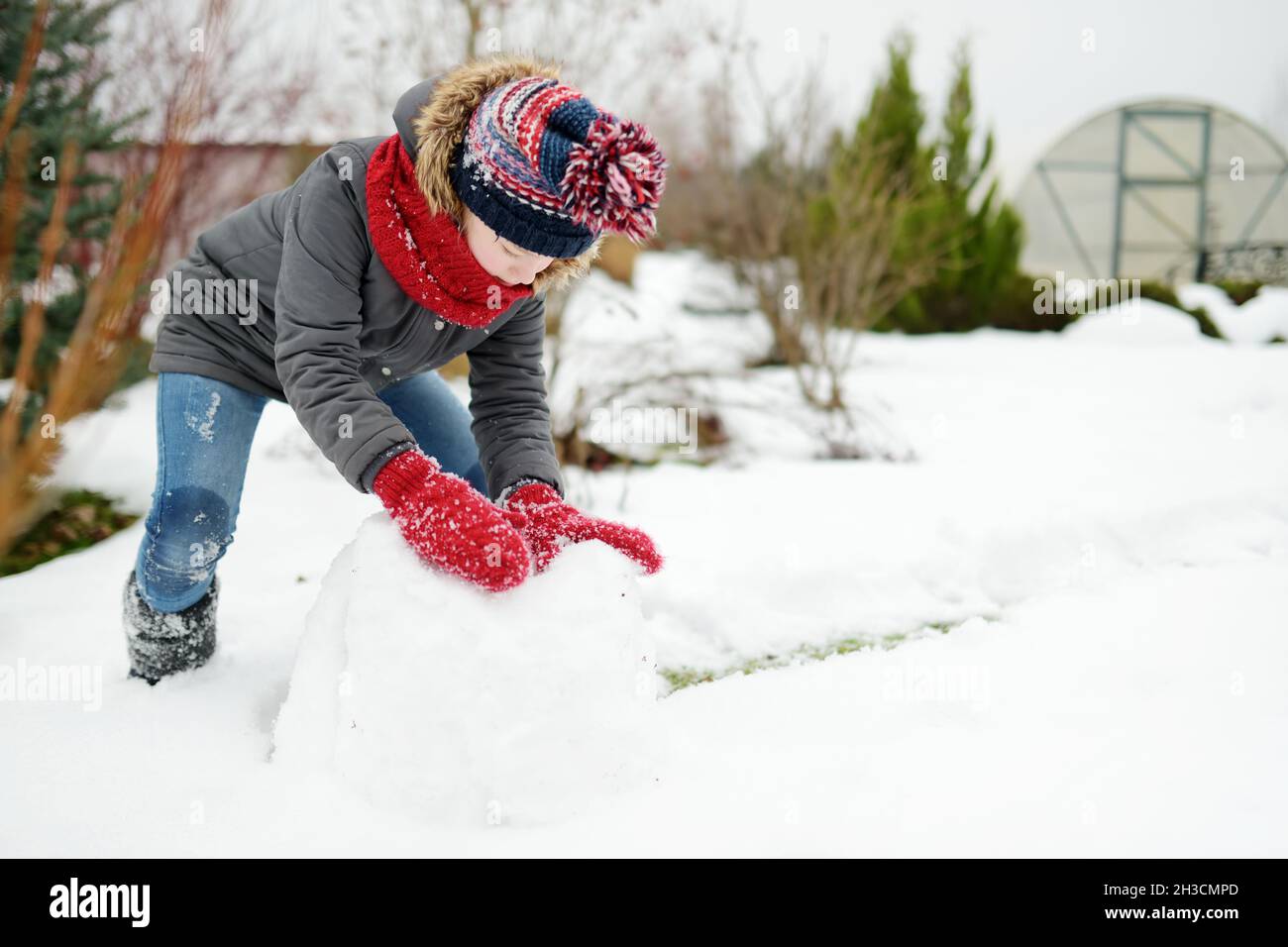 Adorable young girl building a snowman in the backyard. Cute child ...