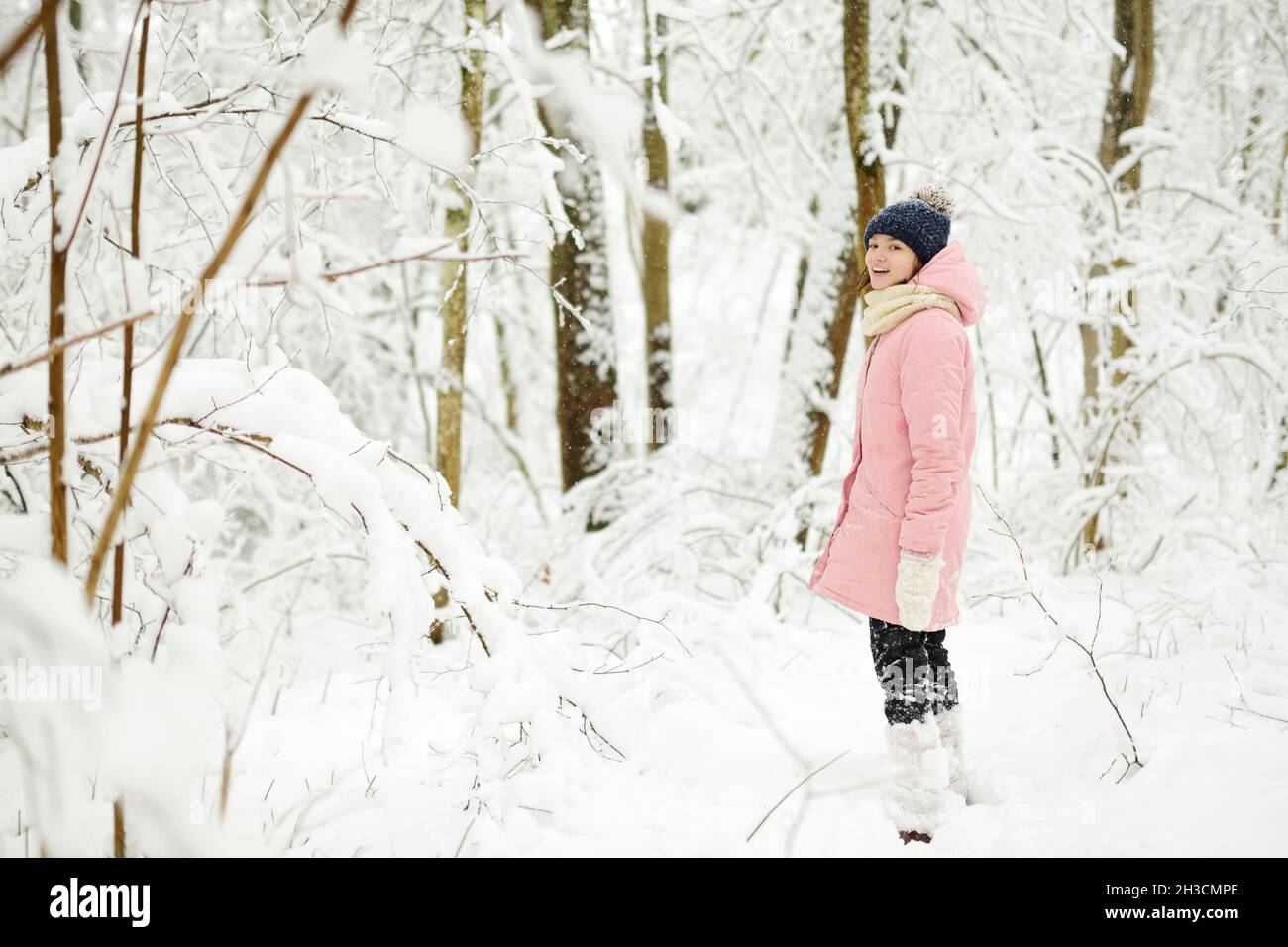 Adorable young girl having fun in beautiful winter park during snowfall ...