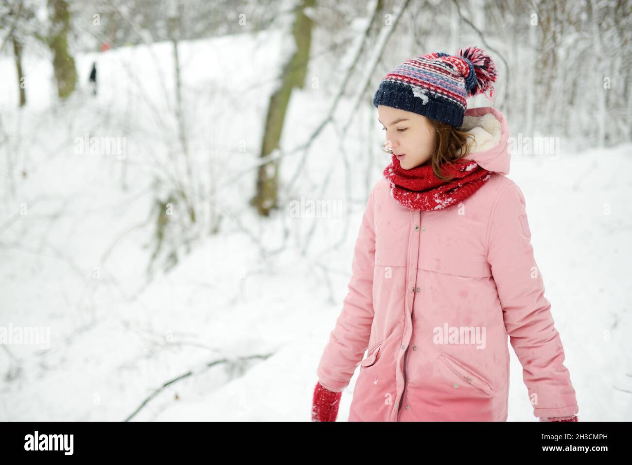 Adorable young girl having fun in beautiful winter park during snowfall ...