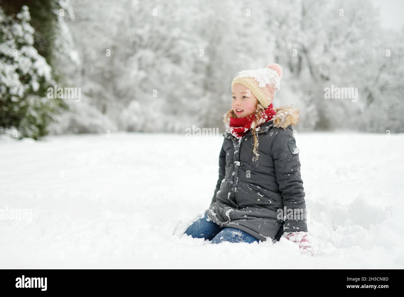 Adorable young girl having fun in beautiful winter park during snowfall ...