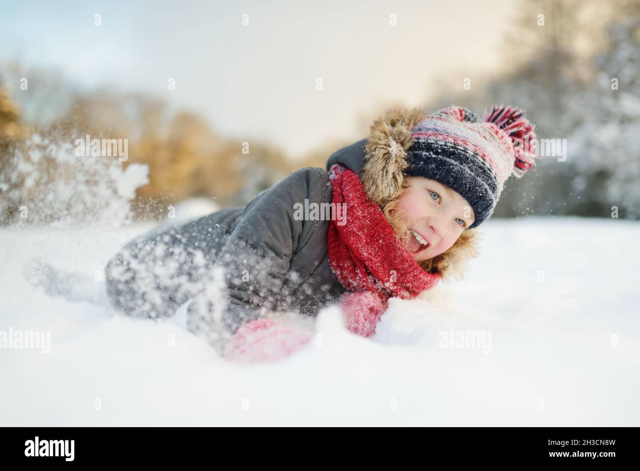 Adorable young girl having fun in beautiful winter park during snowfall ...