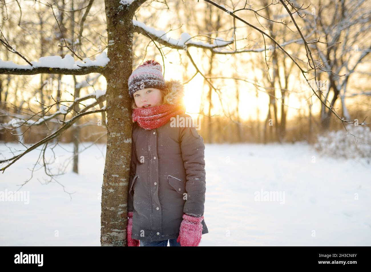Adorable young girl having fun in beautiful winter park during snowfall ...