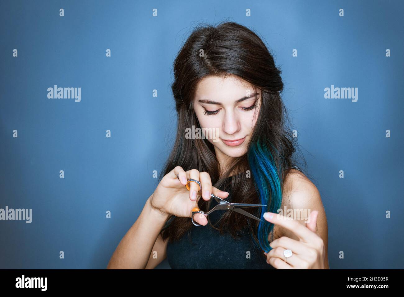 Beautiful brunette woman with a smile cutting long hair with scissors ...