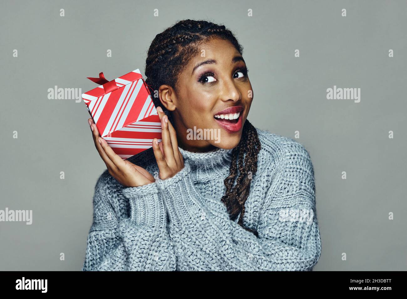 Surprised attractive woman shaking Christmas present on gray background ...
