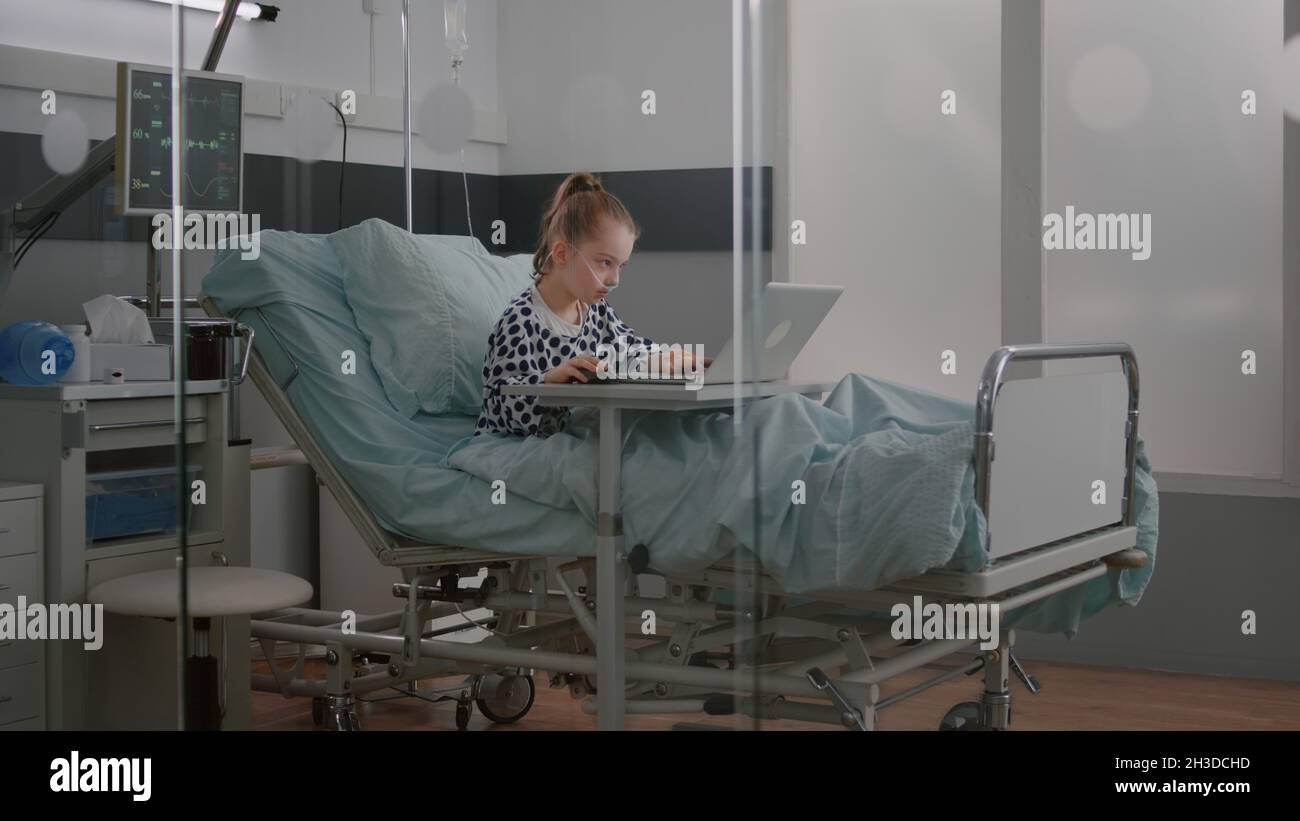 Hospitalized sick girl wearing oxygen nasal tube sitting in bed playing ...