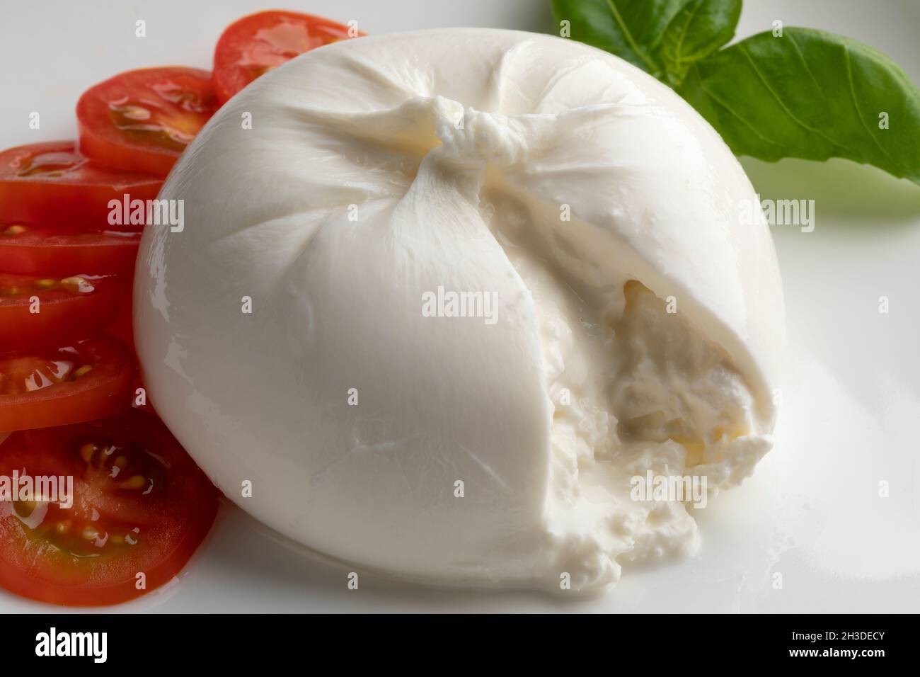Fresh piece burrata cheese close up on white background with tomato ...