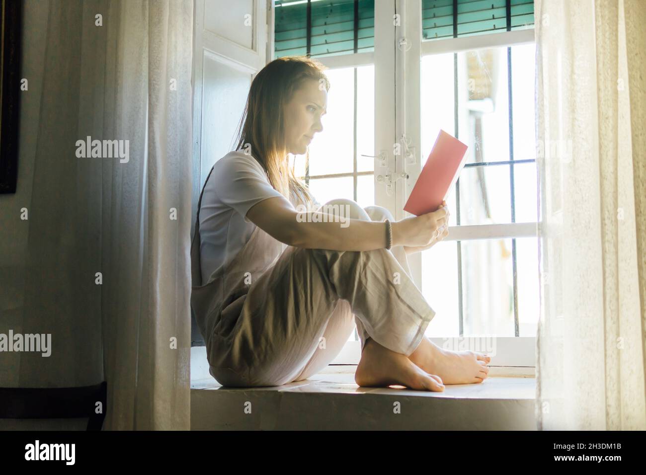 beautiful middle-aged young woman sitting on a window ledge indoors ...