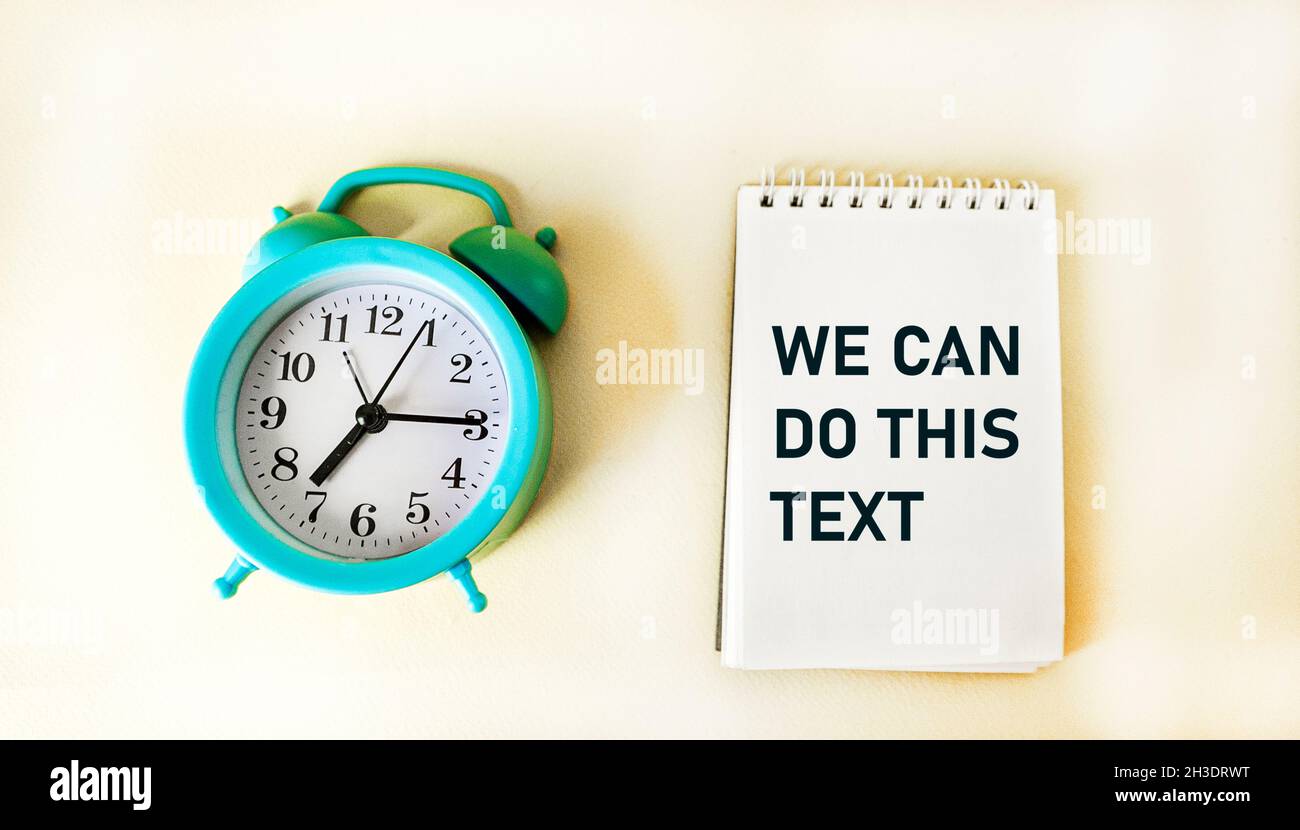 Phrase WE CAN DO THIS TEXT, on notepad and white background with clock ...