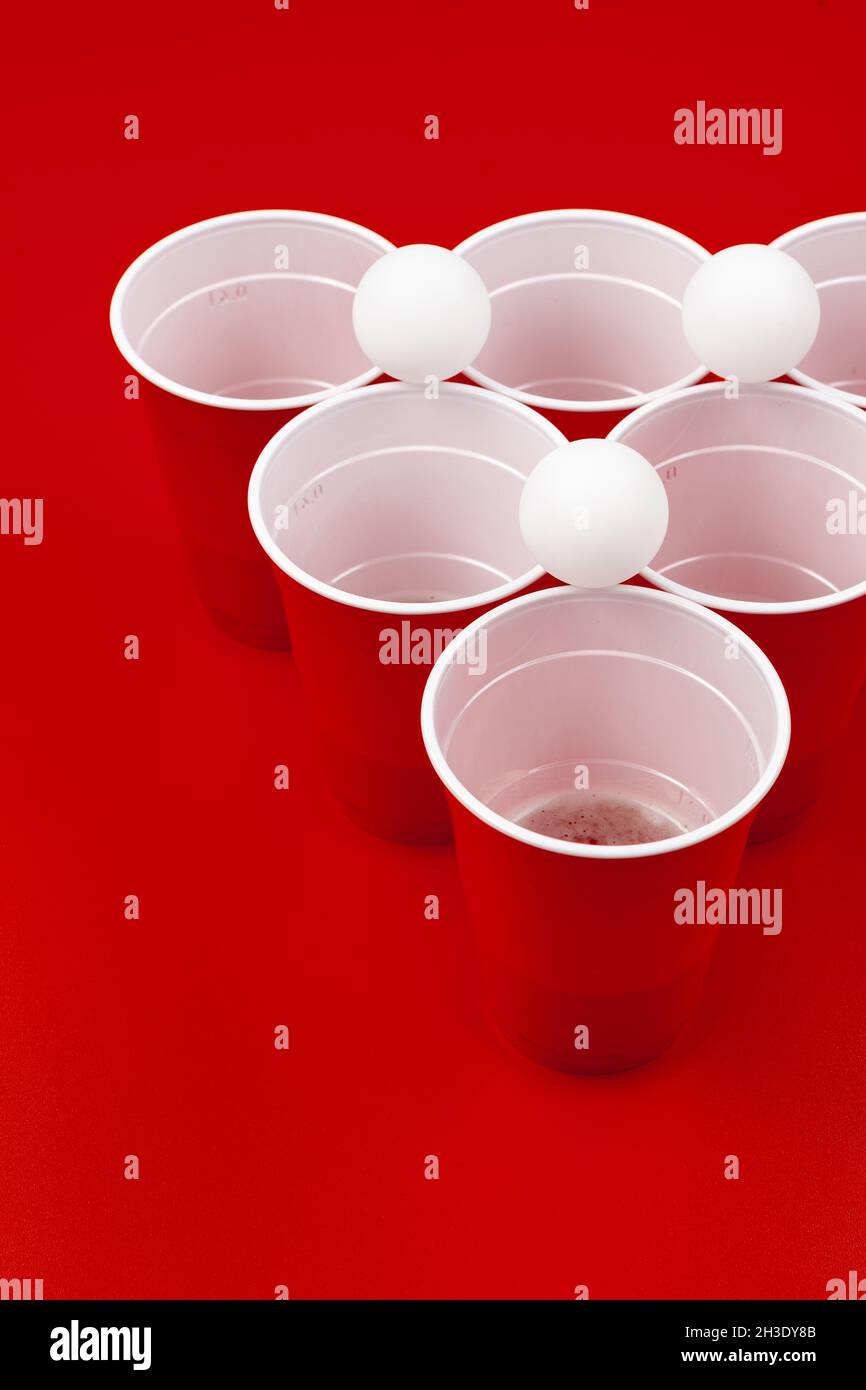 Cups and plastic ball on red background. Beer pong game Stock Photo - Alamy