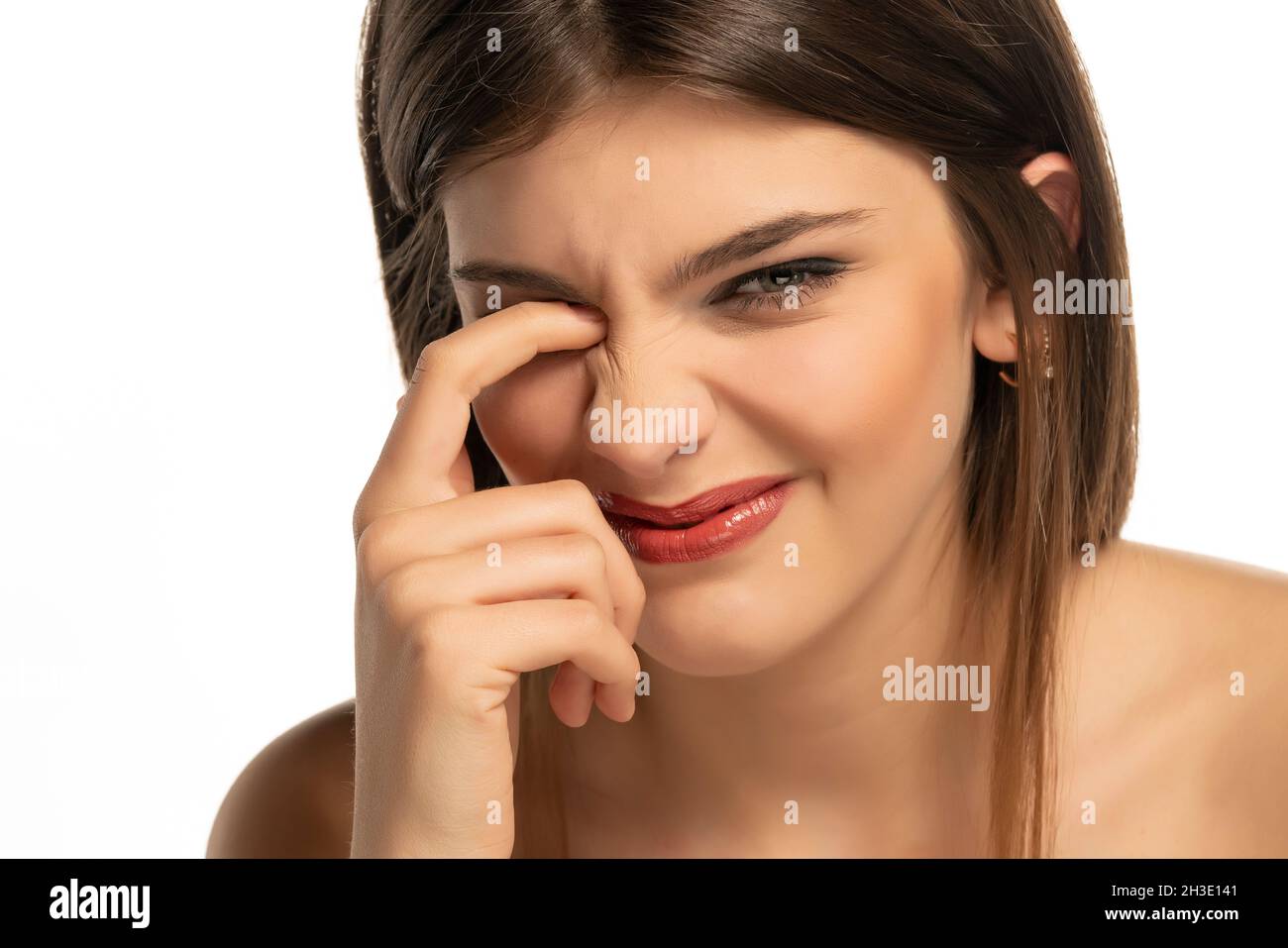 a young beautiful woman scratches her itchy eye on a white background ...