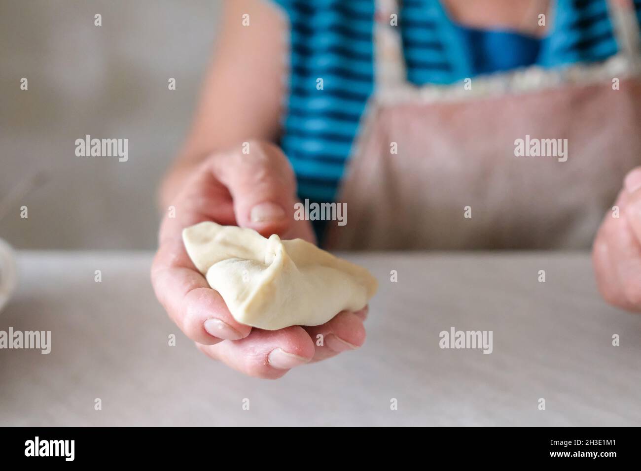 Grandmother holds in her hand a freshly molded manta. A dish of dough ...