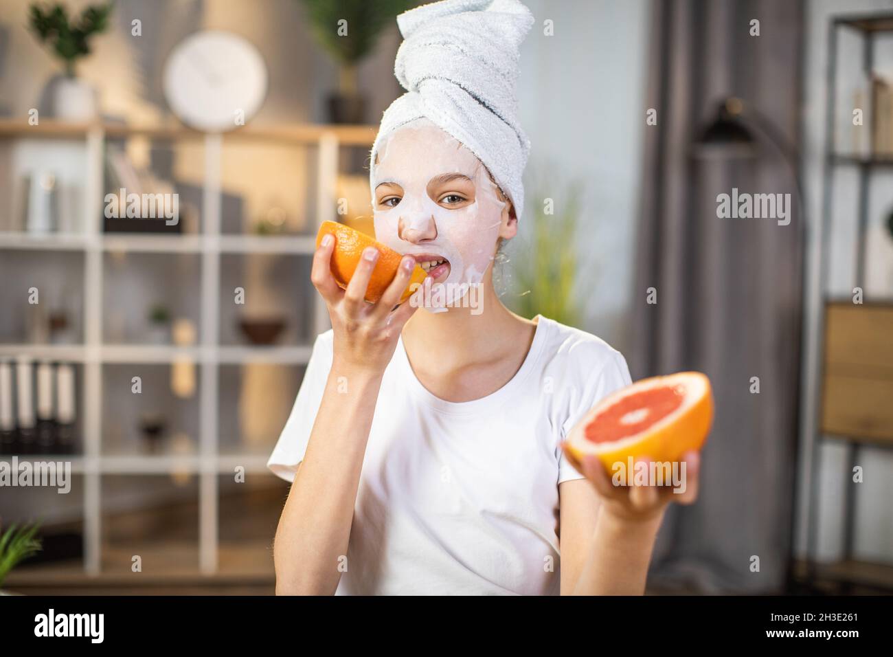 Caucasian female teenager biting slice of grapefruit that while wearing ...