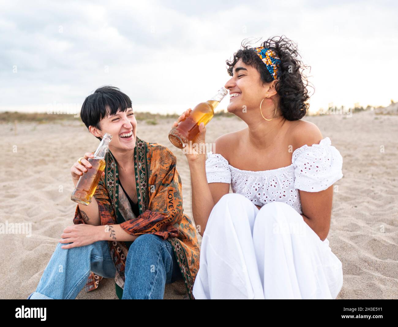 Positive multiethnic female best friends drinking cold beer while ...