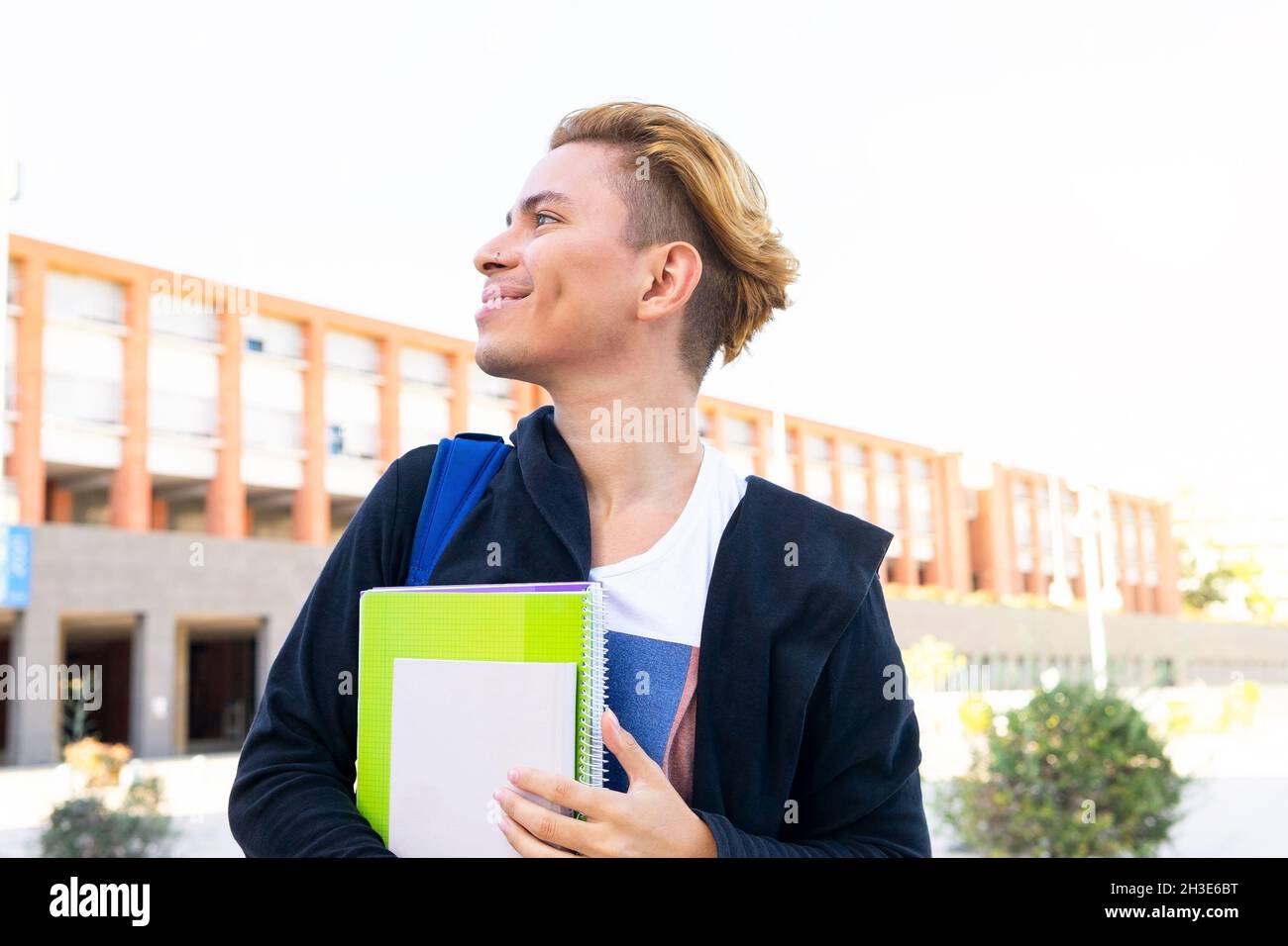Side view of male student with workbooks looking away with thoughtful ...