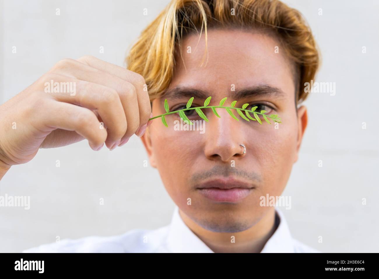 Serious young male in white shirt and small green twig near face ...