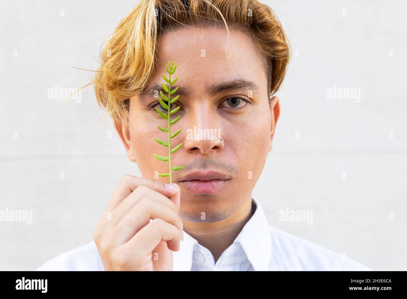 Serious young male in white shirt and small green twig near face ...