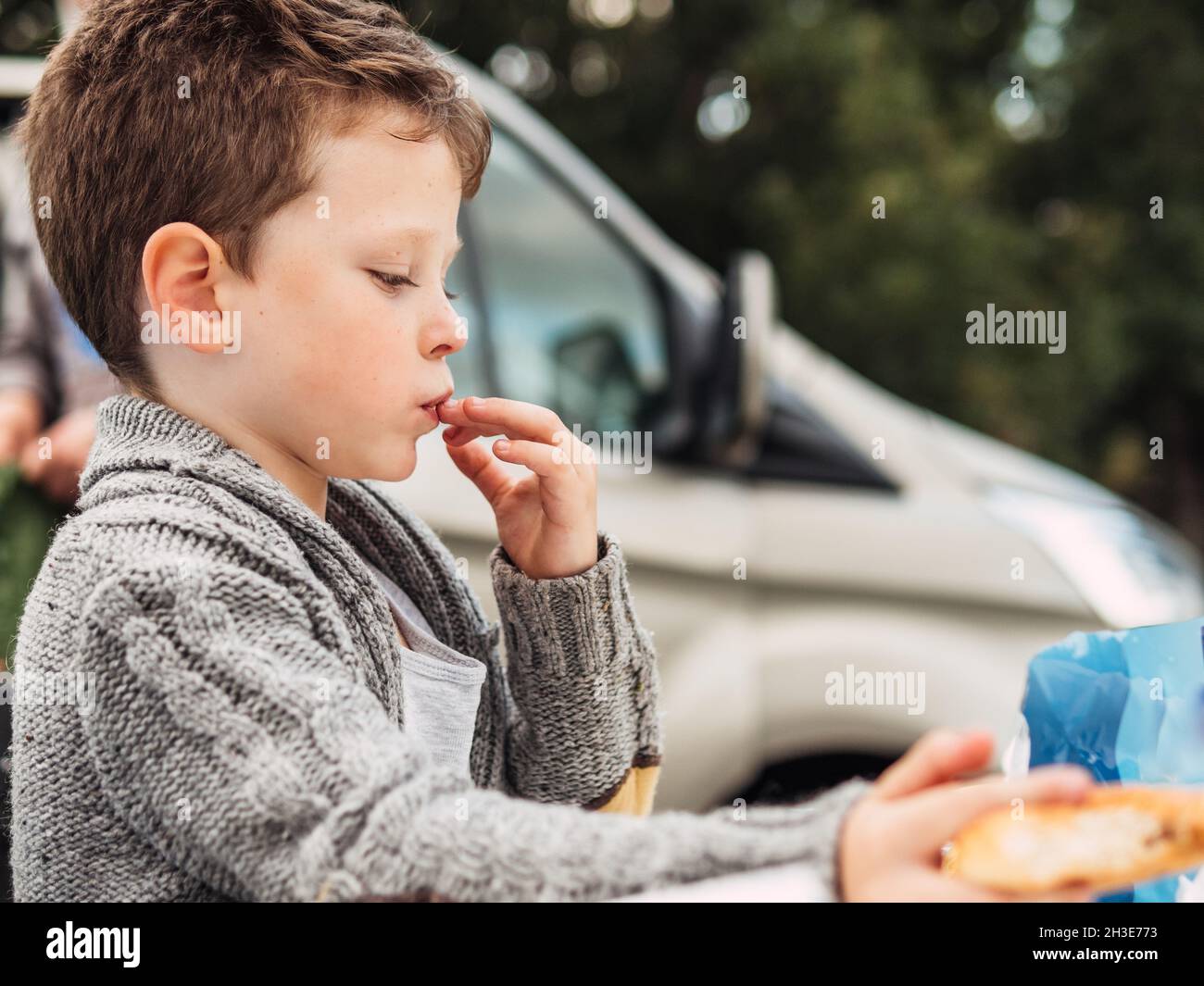 Side view of crop adorable little boy in warm knitted jacket eating ...