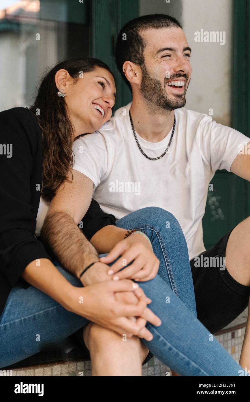 Cheerful young ethnic female in casual clothes cuddling boyfriend while ...