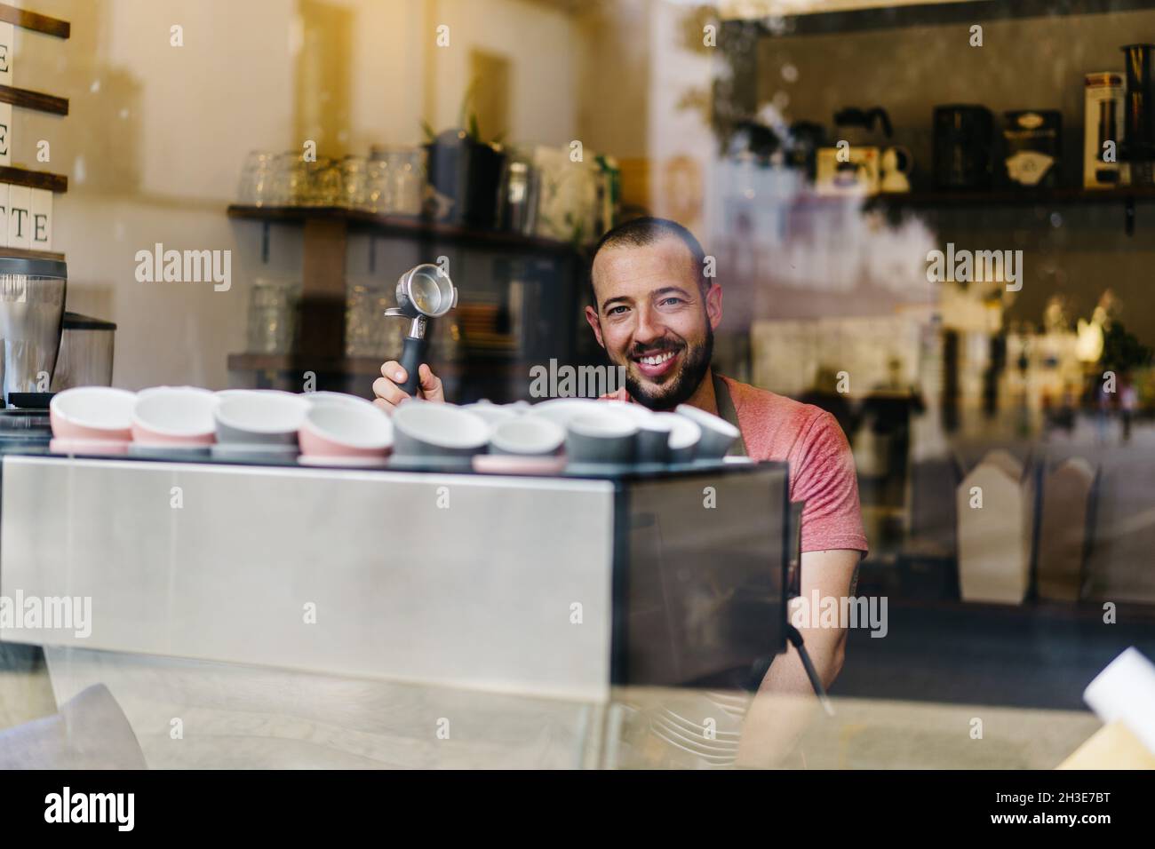 Through glass of male worker in apron preparing coffee while standing ...