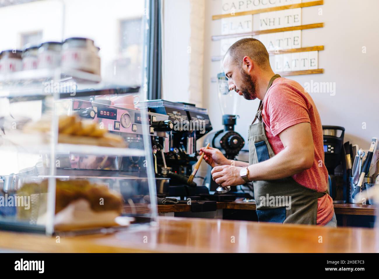Side view of focused male barista in apron cleaning coffee machine with ...