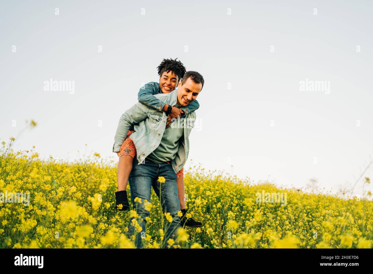 Romantic young man smiling and giving piggyback ride to joyful African ...