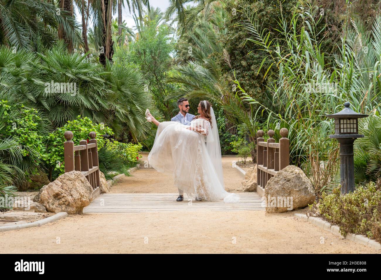 Full body of groom holding bride in white dress in hands while standing ...