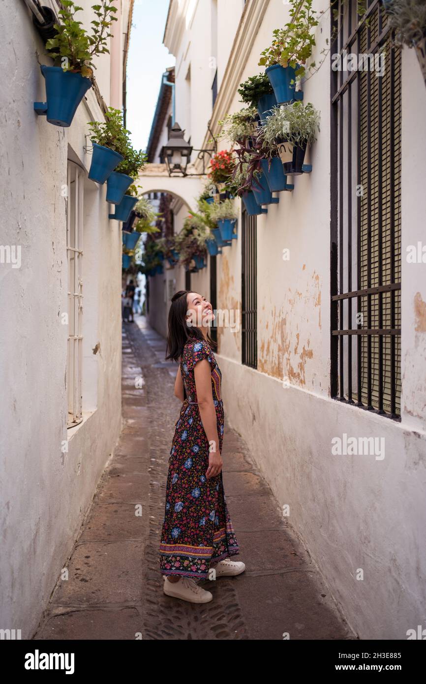 Full body side view of smiling Asian female tourist standing in narrow ...