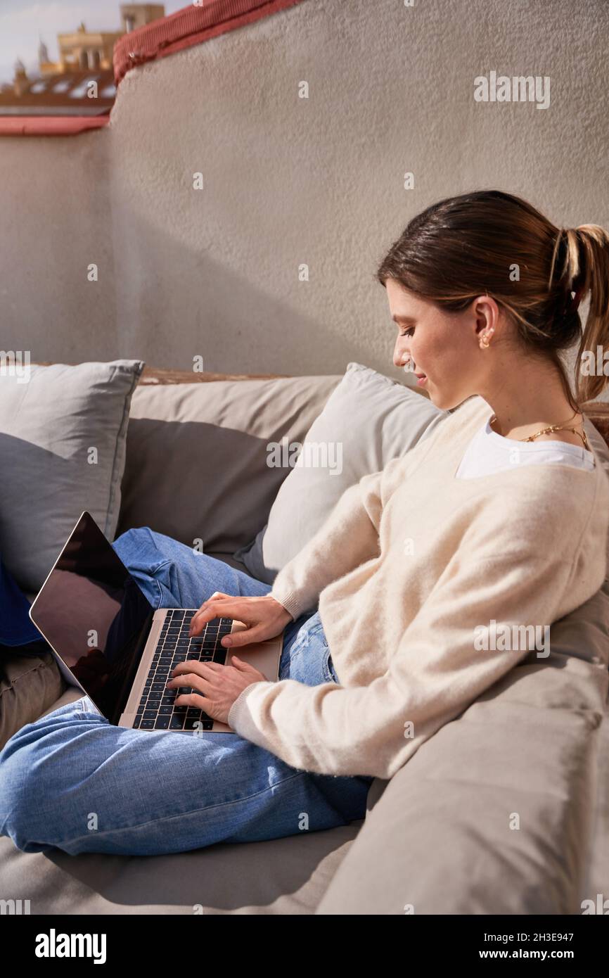 Side view of young female sitting with crossed legs using modern ...