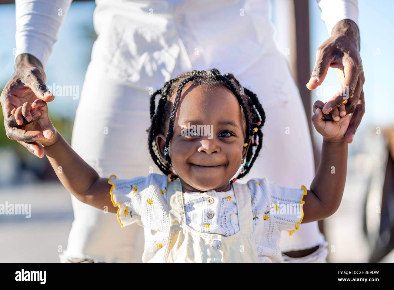 Happy African American little girl in light dress holding hands of ...
