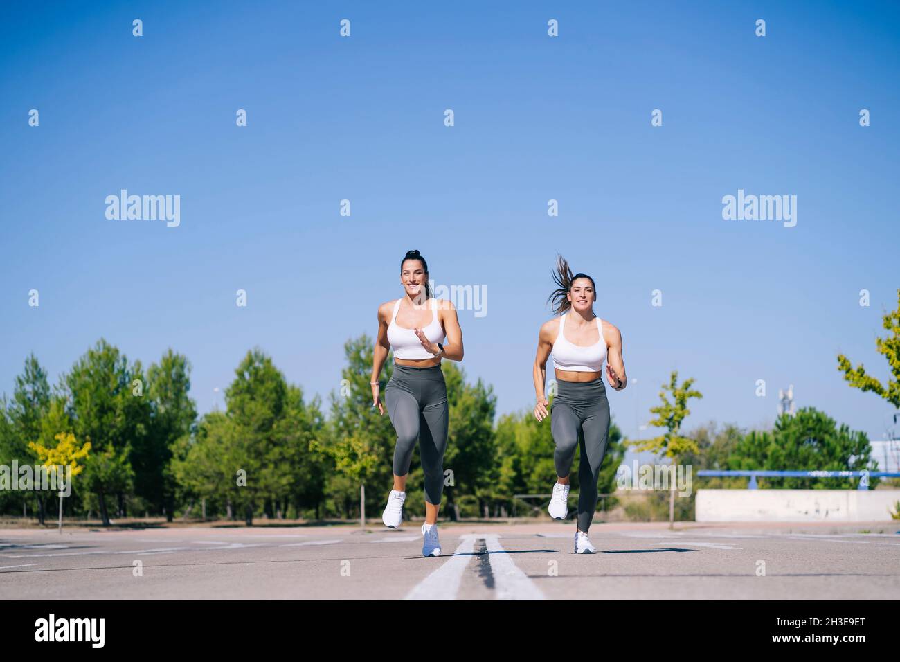 Full body of smiling sporty female twins in sportswear running together ...