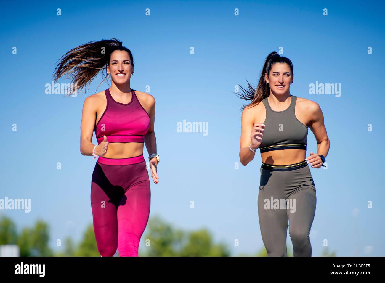 Sporty twins running fast on asphalt road during workout under blue sky ...