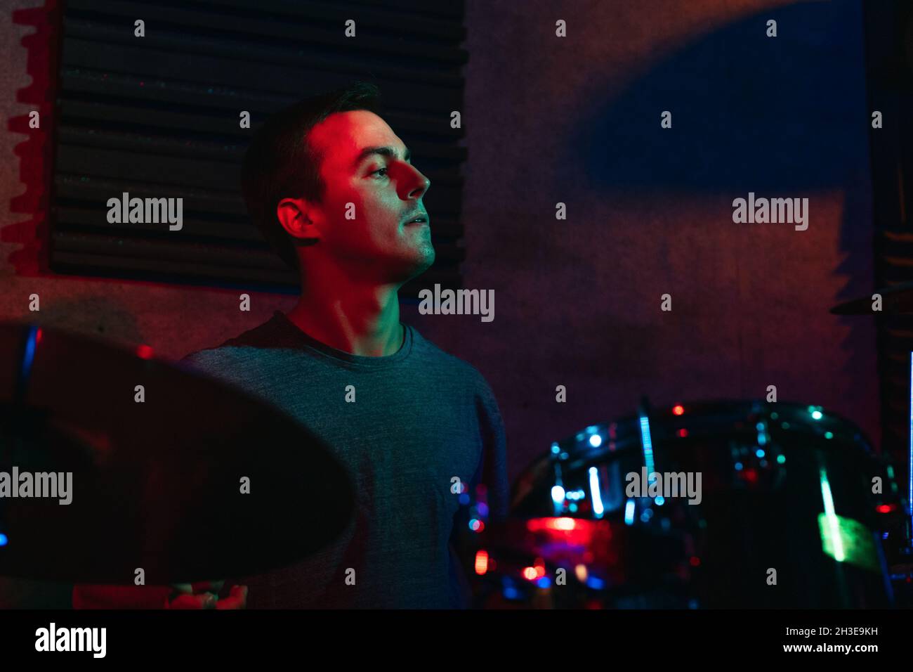 Concentrated young male musician playing drums in club with green and ...