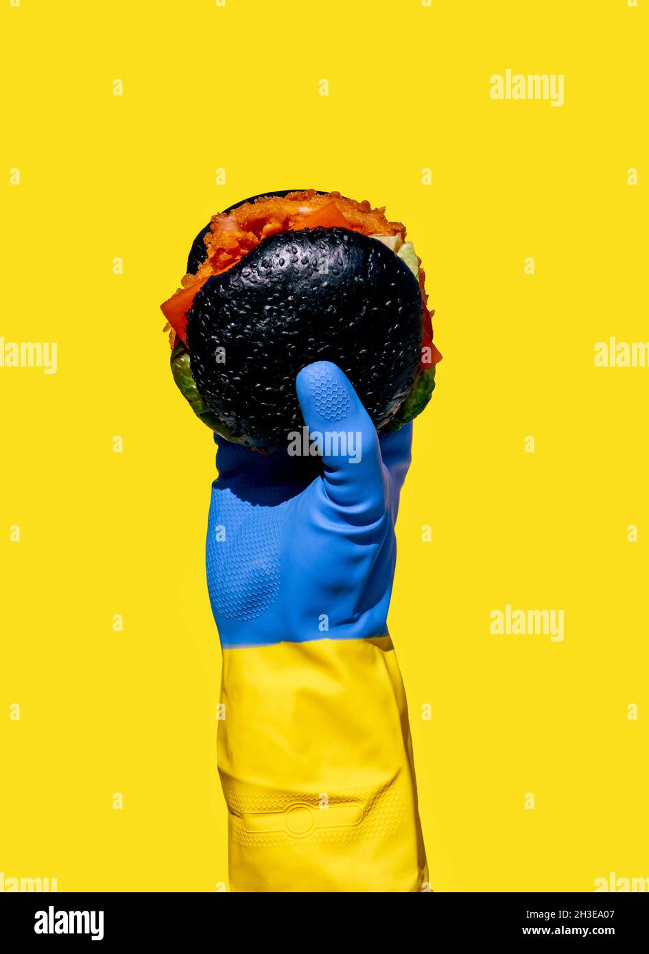 Crop person in colorful rubber glove demonstrating burger with black ...