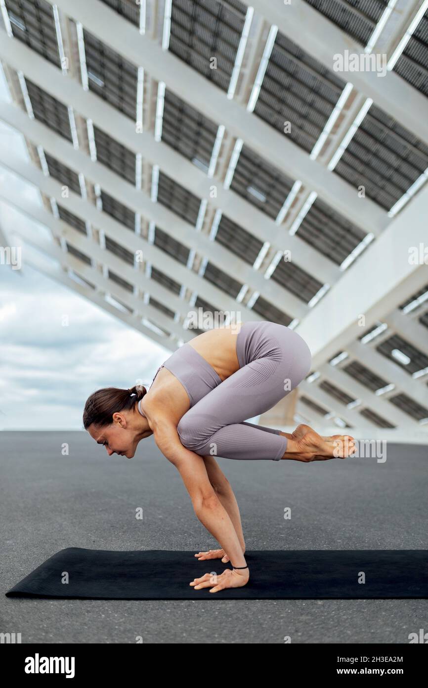 Full body of female doing crow posture on mat on street near solar ...