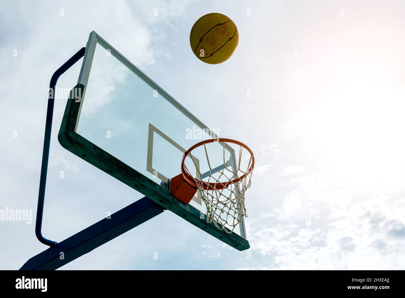 From below of basketball flying in hoop with backboard against blue sly ...