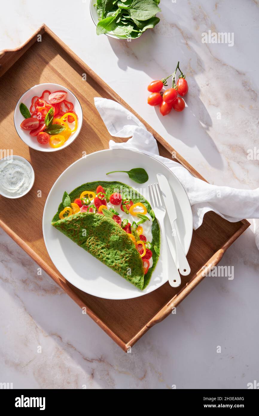 Overhead of spinach creppe with tomato and pepper slices served on ...