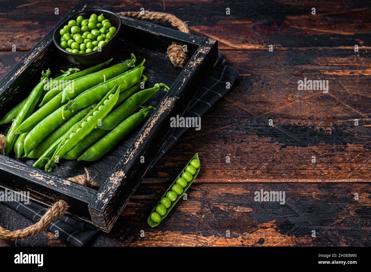 Raw green pea pods in a wooden tray. Dark wooden background. Top view ...