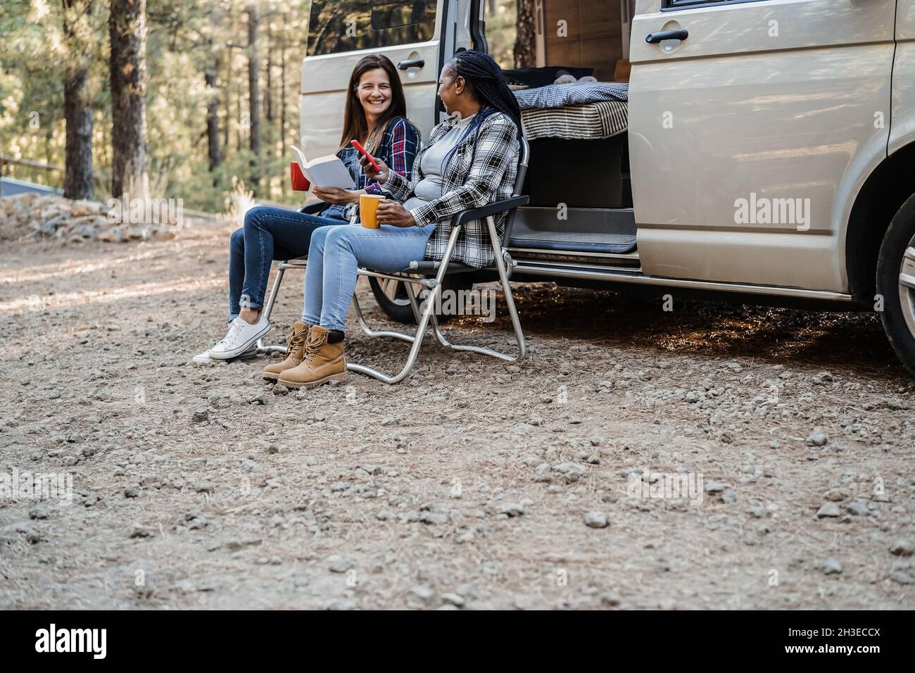 Multiracial women friends having fun camping with camper van while ...